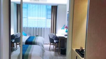 Quarto de hotel com duas camas, uma escrivaninha, uma cadeira e uma janela com cortinas.