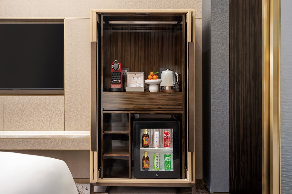 Minibar com cafeteira, pequeno frigorífico com bebidas e uma cesta de frutas.