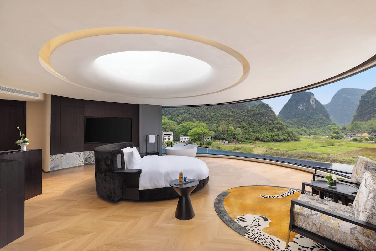 Quarto moderno com uma cama grande, uma escrivaninha e vista para uma paisagem montanhosa.
