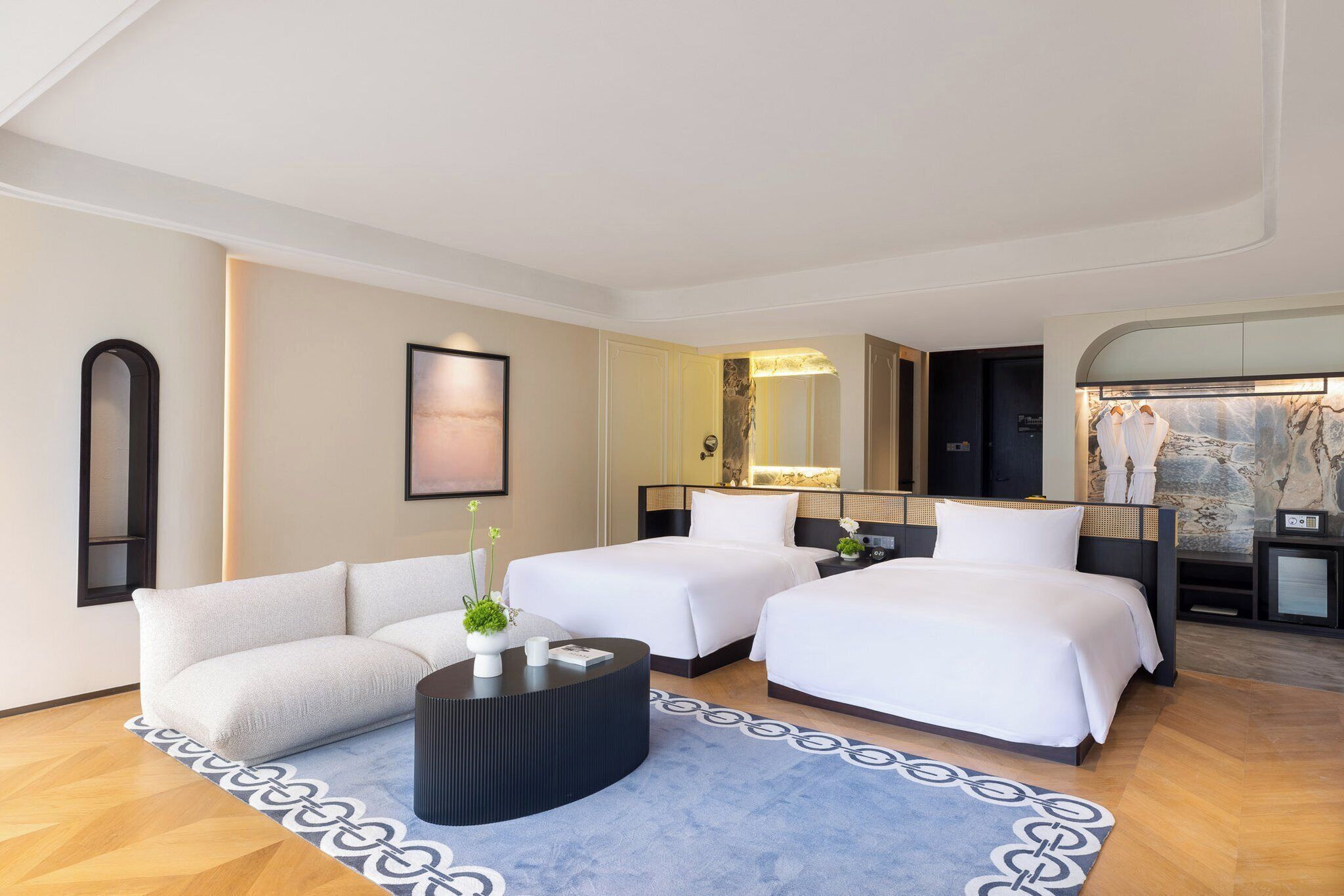 Quarto de hotel com duas camas, um sofá, uma mesa de centro redonda e um espelho grande.