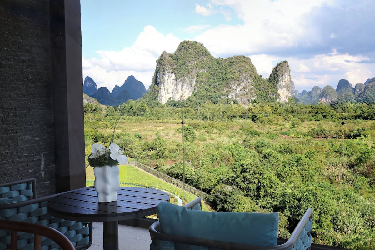 Uma varanda com mesa e cadeiras, com vista para uma paisagem exuberante e formações calcárias.