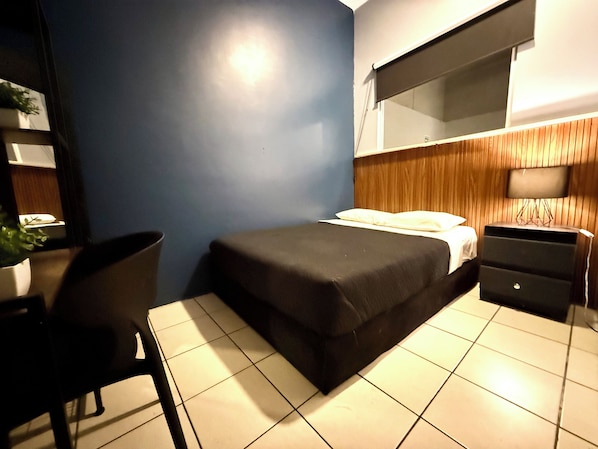 Quarto com cama, escrivaninha, cadeira, cómoda e planta em vaso.