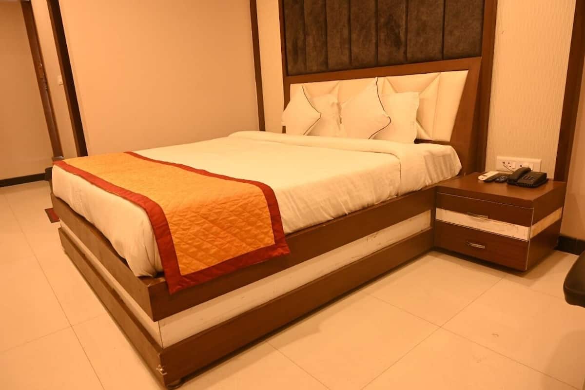 Cama bem arrumada com edredom acolchoado, mesa de cabeceira com telefone e mesa de apoio com abajur.