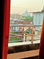 Vista de uma varanda com guarda-corpo de metal, com vista para uma área residencial com vários edifícios, incluindo uma mesquita com cúpula.