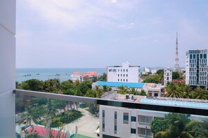 Vista de uma varanda com vista para a costa, edifícios, céu claro e um corpo de água.