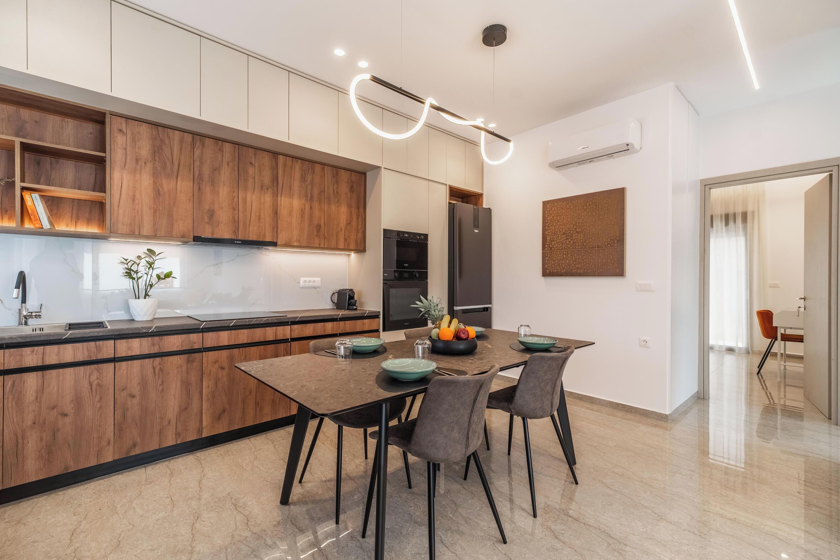 Uma cozinha moderna com armários de madeira, bancada de mármore e um espaço de refeições com mesa e cadeiras.
