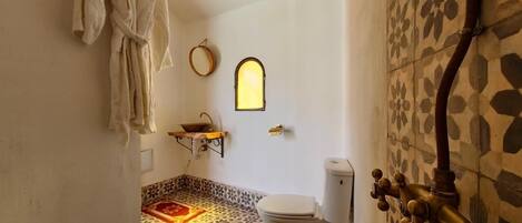 Casa de banho com sanita, lavatório, chuveiro e chão estampado.
