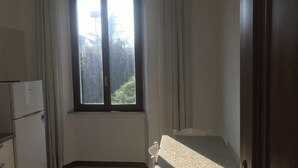 Uma cozinha pequena com geladeira, uma janela com cortinas e uma mesa com cadeiras.