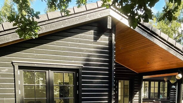 Uma cabana moderna com grandes portas de correr de vidro, um alpendre coberto com móveis de exterior e um telhado inclinado.