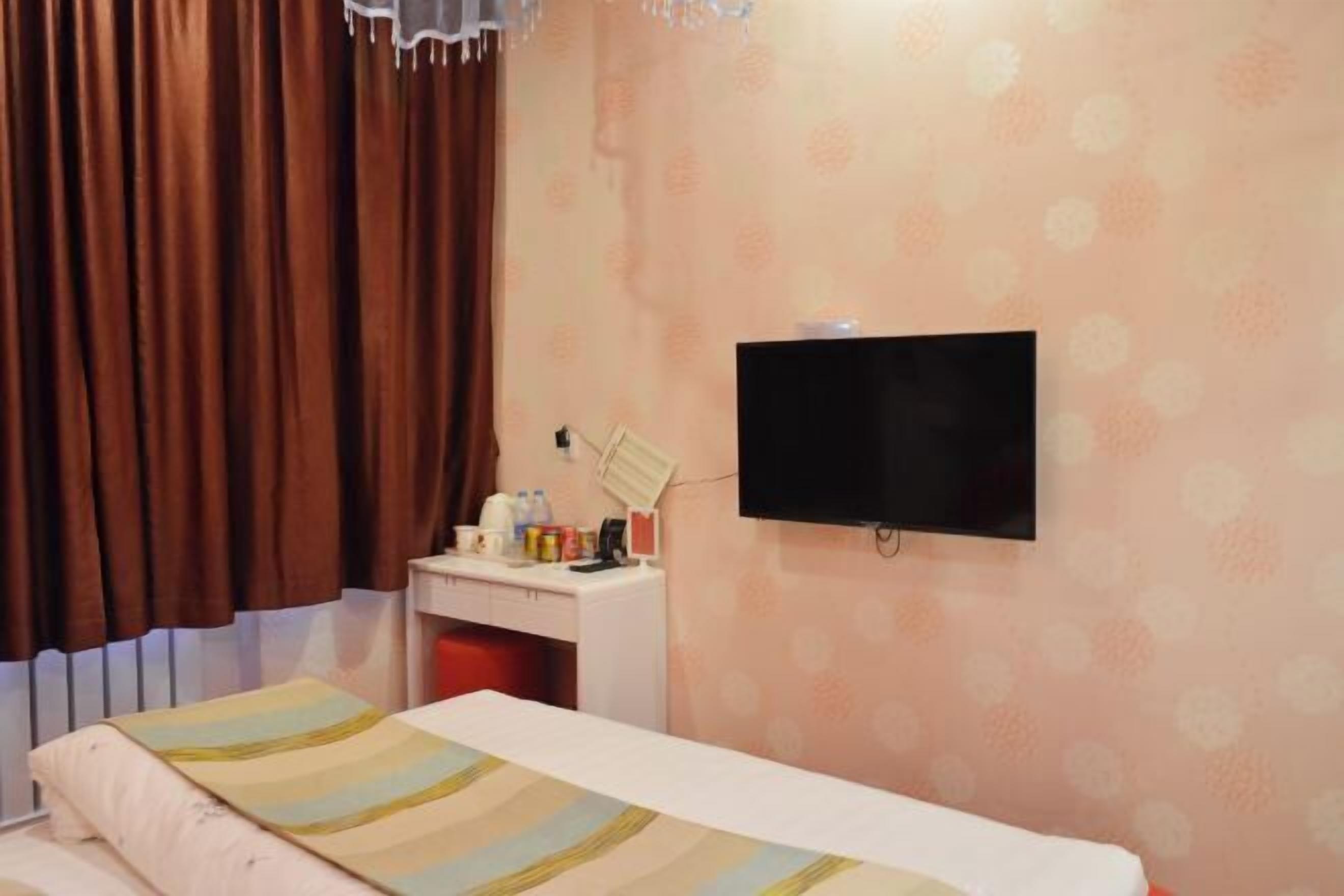 Quarto de hotel com cama, escrivaninha, televisão e janela com cortinas.