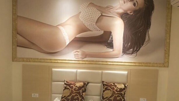 Quarto de hotel com cama, duas almofadas decorativas e uma obra de arte na parede.