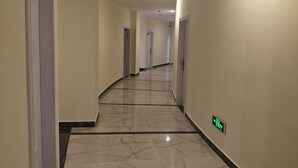 Um corredor comprido e estreito com chão de mármore e portas em ambos os lados.