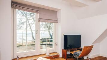 Quarto com uma janela grande, televisão de tela plana, piso de madeira e sofá branco.