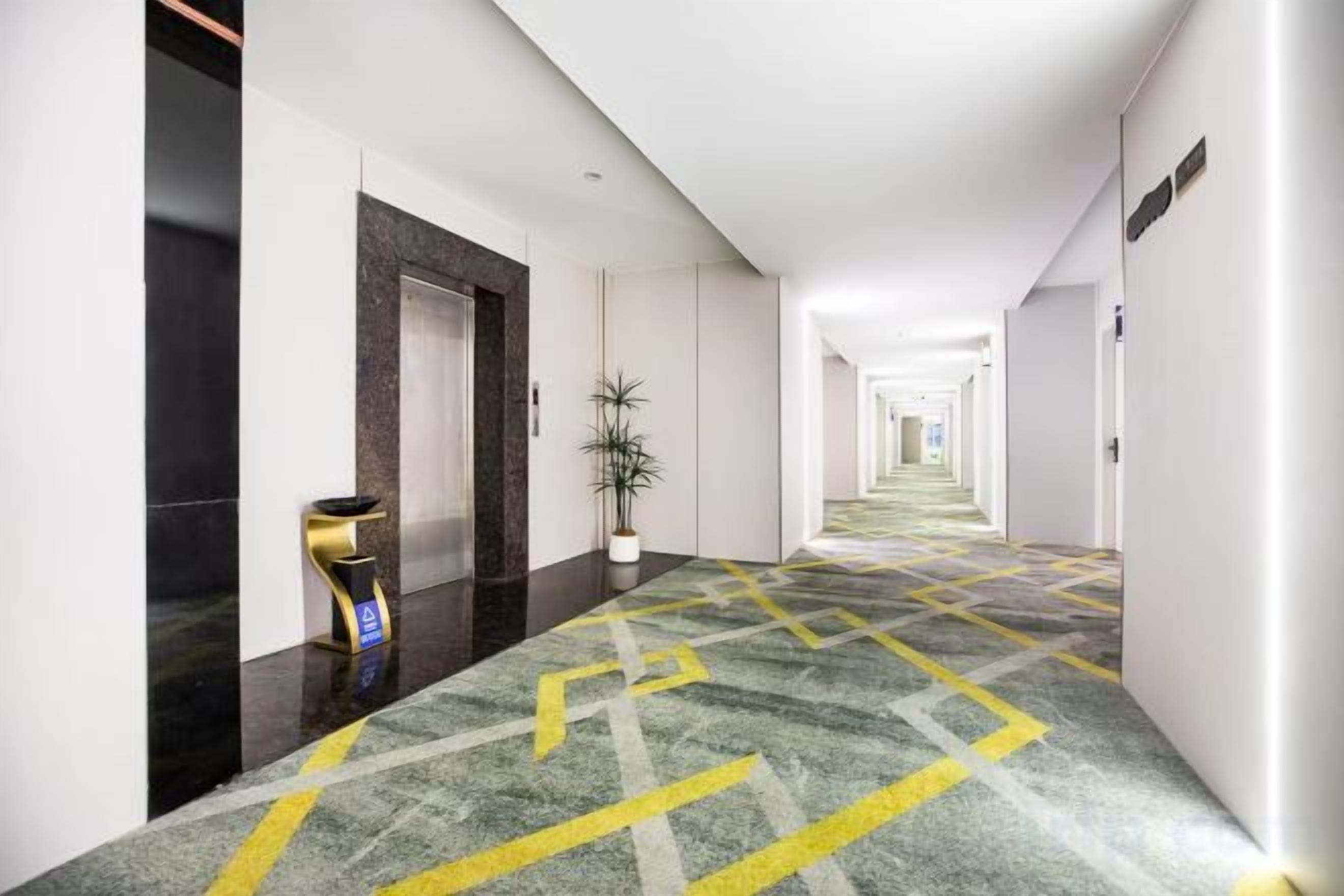 Corredor de hotel com carpete estampado, balcão de recepção e planta em vaso.