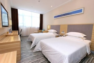 Quarto de hotel com duas camas, uma escrivaninha, uma cadeira, uma televisão e uma janela com cortinas.