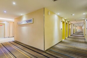 Corredor de hotel com piso coberto por carpete, portas e um quadro na parede.