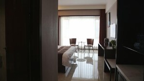 Quarto de hotel com cama, duas cadeiras, uma mesinha, televisão e varanda com cortinas.