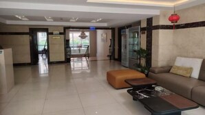 Um hall de hotel com balcão de recepção, área de estar com sofá e apoio para os pés, mesa de jantar e uma janela ampla.