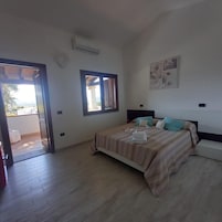 Quarto com cama, janela e porta que dá para área externa.