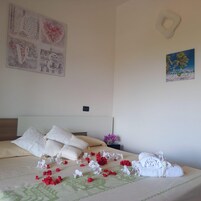 Cama bem arrumada com almofadas, uma toalha enrolada e pétalas de flores espalhadas.