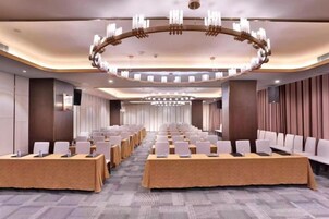 Uma sala de conferências com mesas, cadeiras dispostas em fileiras e um grande lustre.