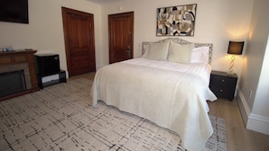 Quarto com cama, duas portas, lareira, obra de arte na parede e abajur.