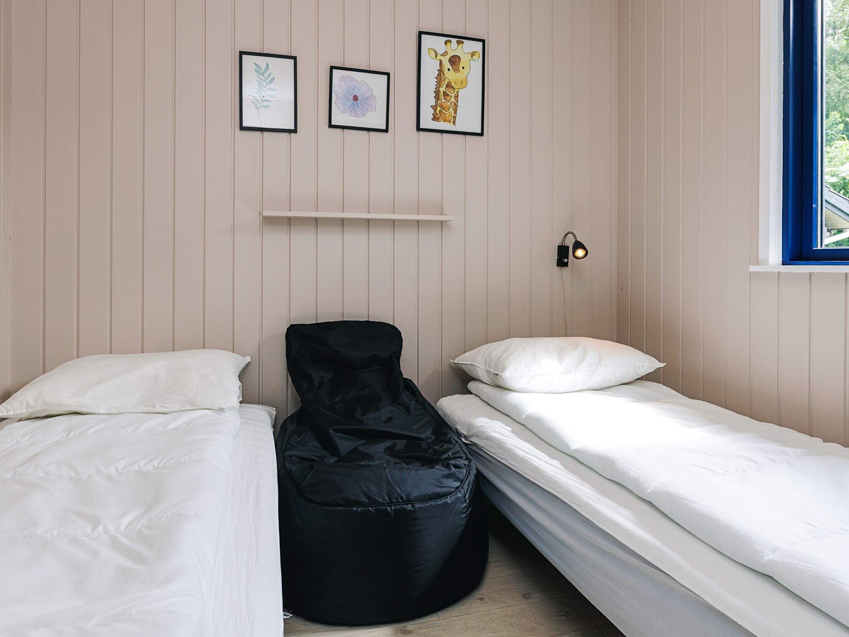 Quarto com duas camas de solteiro, uma poltrona de couro preta e três quadros na parede.