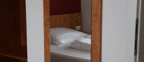 Cama de solteiro com roupa de cama branca num quarto com cabeceira de madeira e parede com destaque em vermelho.
