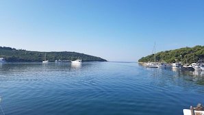Água calma com barcos, céu claro e paisagem montanhosa ao longe.