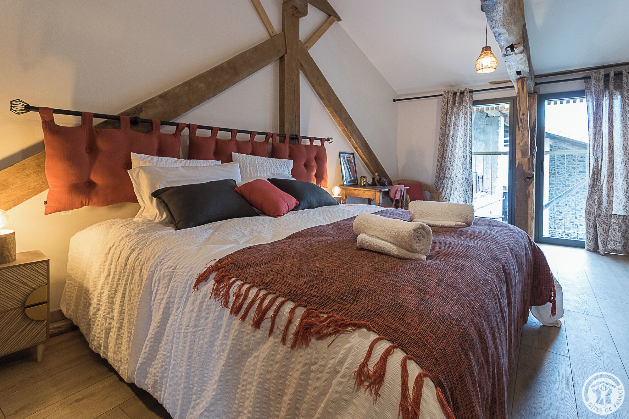 Um quarto espaçoso com uma cama grande, vigas de madeira, vista para o exterior e uma janela com cortinas.