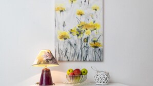 Um armário branco com uma luminária, uma tigela de frutas e um objeto decorativo em cima.