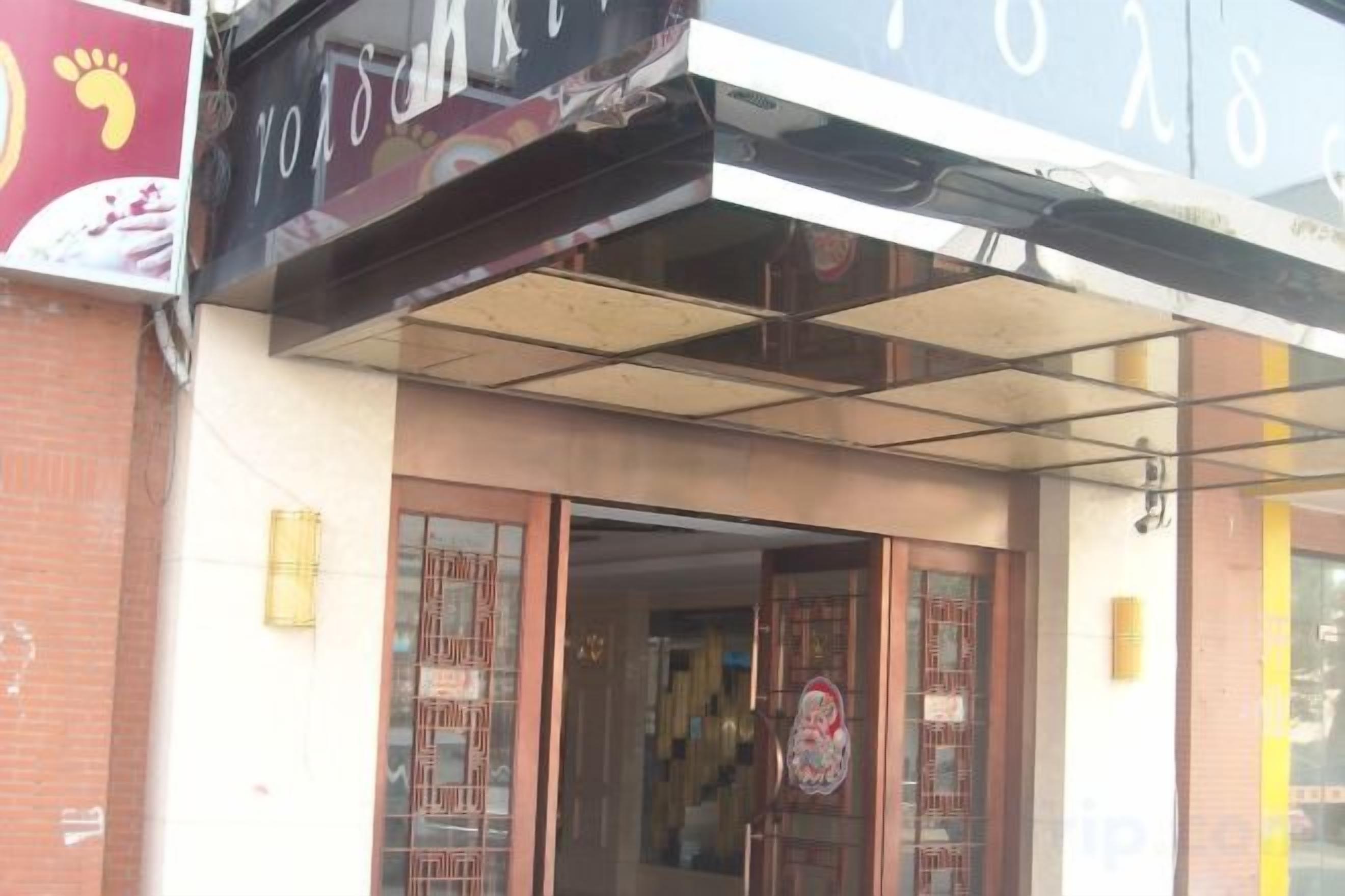 Fachada de loja com placa sobre a entrada, porta com painéis de vidro e uma pequena cobertura.