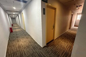 Corredor de hotel com piso coberto por carpete, porta de madeira e extintor de incêndio.