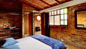 Quarto com cama, parede de tijolos, teto de madeira e janela.