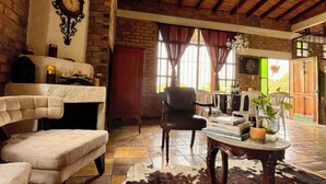 Um interior rústico com teto de madeira, tapete de couro, mesa de jantar com livros e uma poltrona de couro.