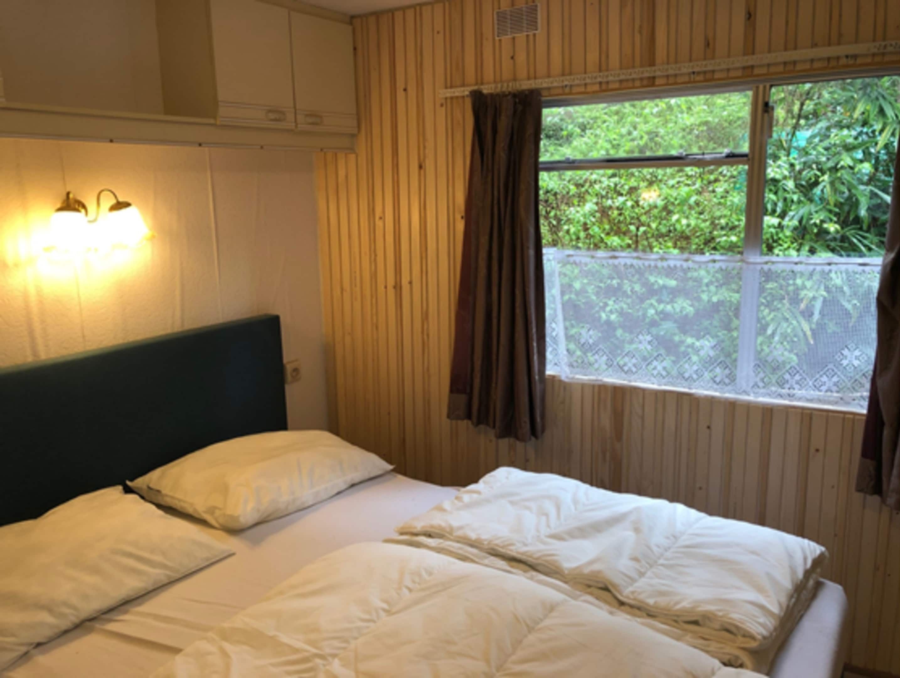 Cama com roupa de cama branca, cabeceira e janela com cortinas.