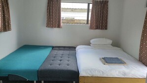 Quarto individual com uma cama, um banco e uma janela.