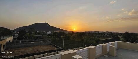 Vista do pôr do sol de um terraço, com uma colina ao fundo.