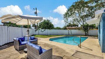 Um quintal com piscina, móveis de vime e guarda-sóis.