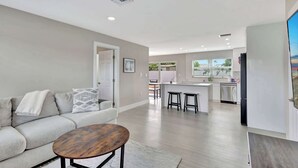 Uma sala de estar moderna com um sofá, uma mesa de centro e uma cozinha ao fundo.
