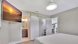 Quarto com uma cama grande, uma porta para um banheiro e vista para uma cozinha.