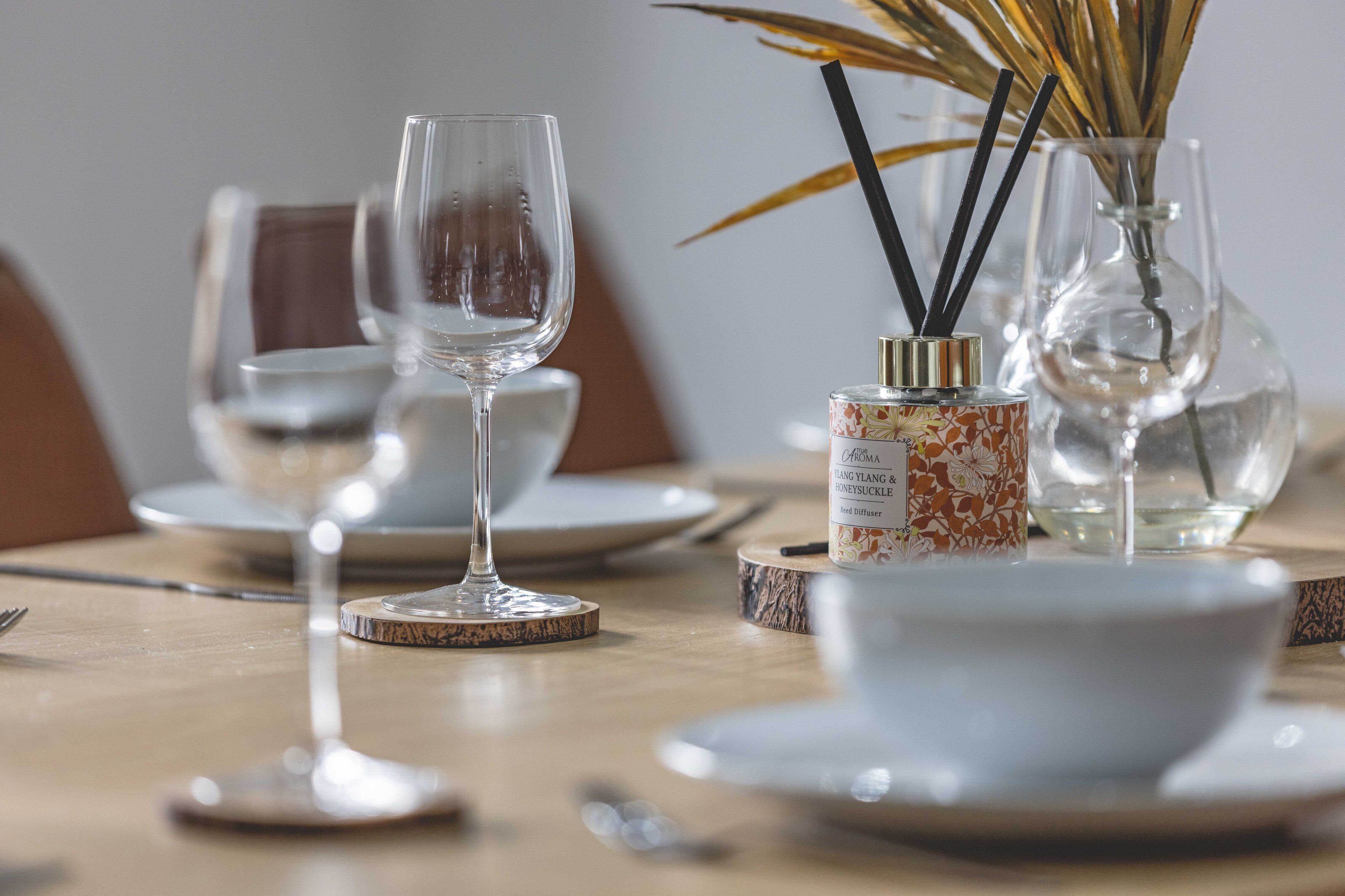 Uma mesa de jantar posta com copos de vidro transparente, um castiçal decorativo e um vaso com plantas secas.
