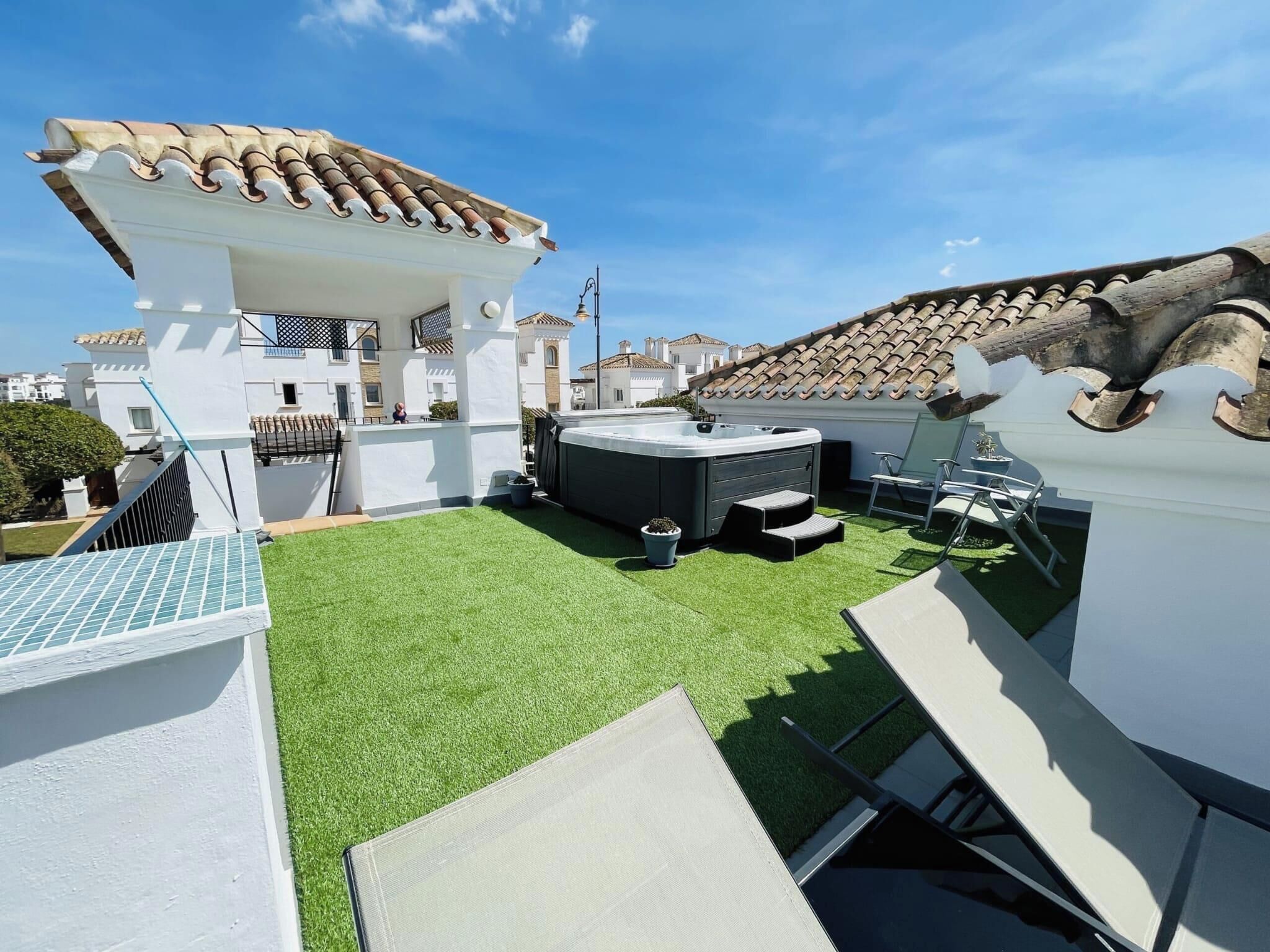 Terraço no telhado com grama sintética, banheira de hidromassagem e área de estar externa.