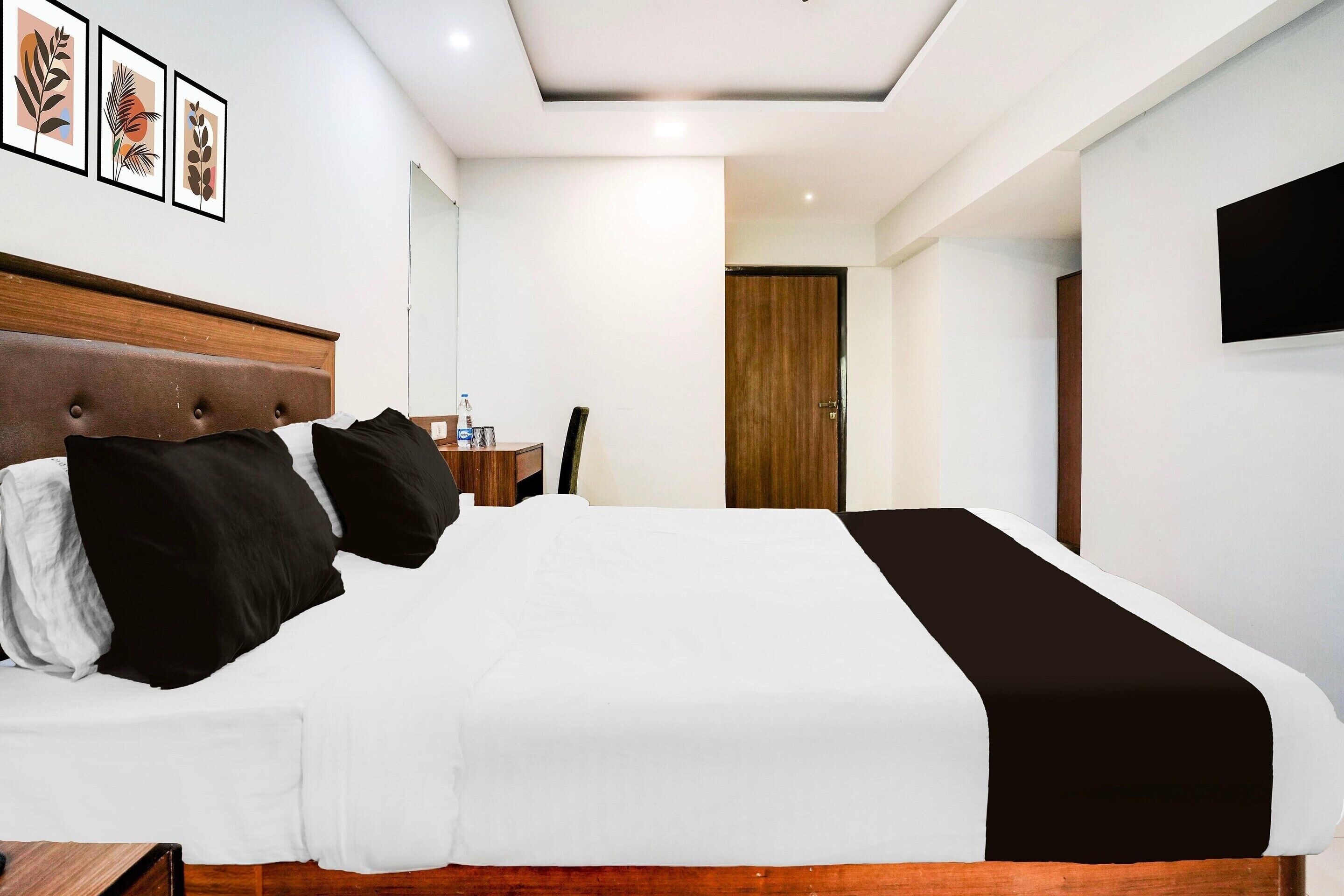 Quarto de hotel com uma cama grande, cabeceira de madeira, televisão de tela plana na parede e obras de arte emolduradas acima da cama.