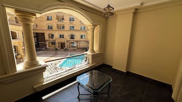 Varanda com mesa de vidro e vista para um pátio com colunas e piscina.