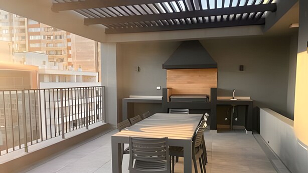 Um terraço no último andar com uma mesa comprida e cadeiras, uma churrasqueira e uma pérgula.