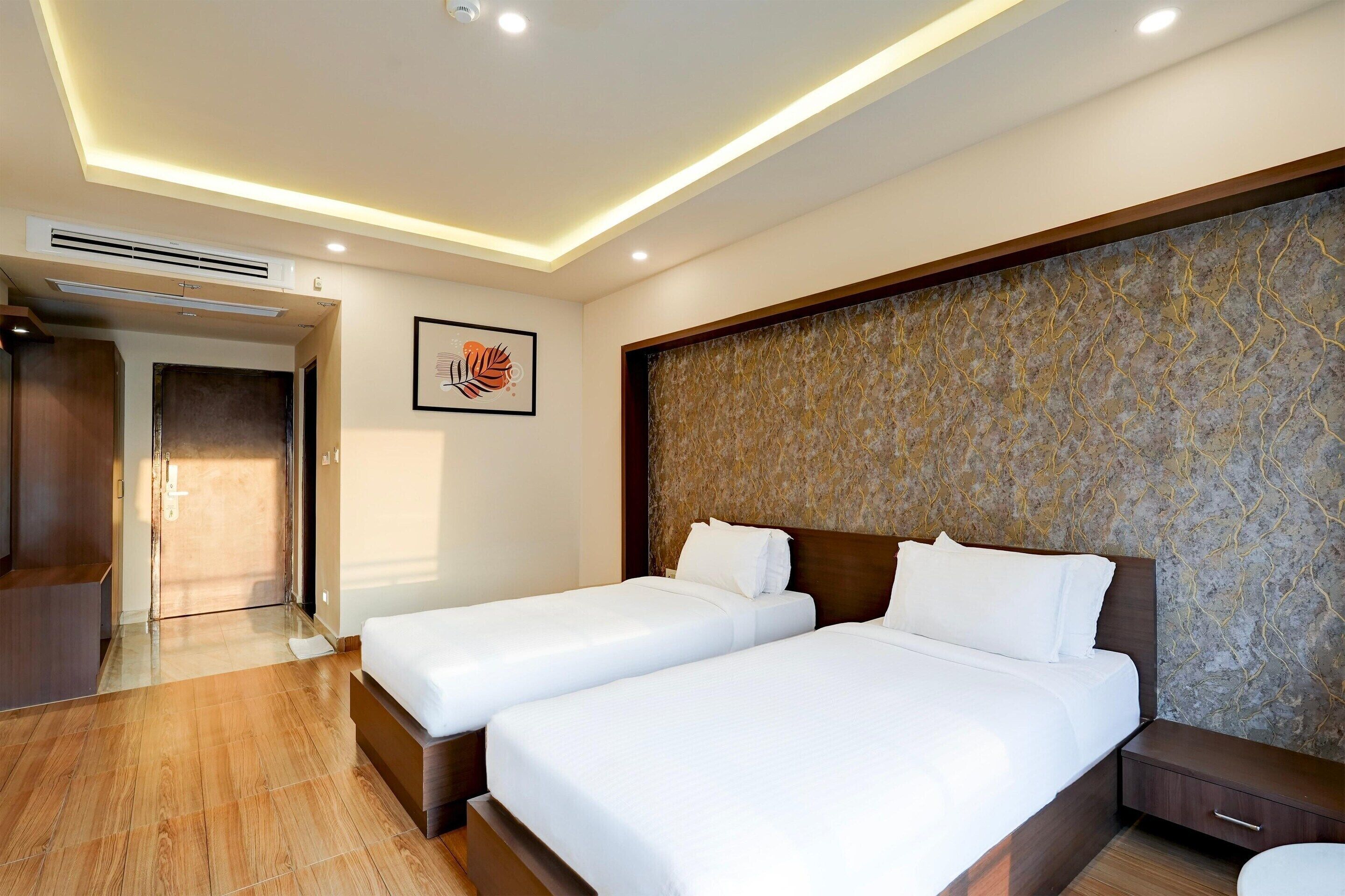 Quarto de hotel com duas camas, piso de madeira, parede com padrão marmorizado e teto com iluminação embutida.
