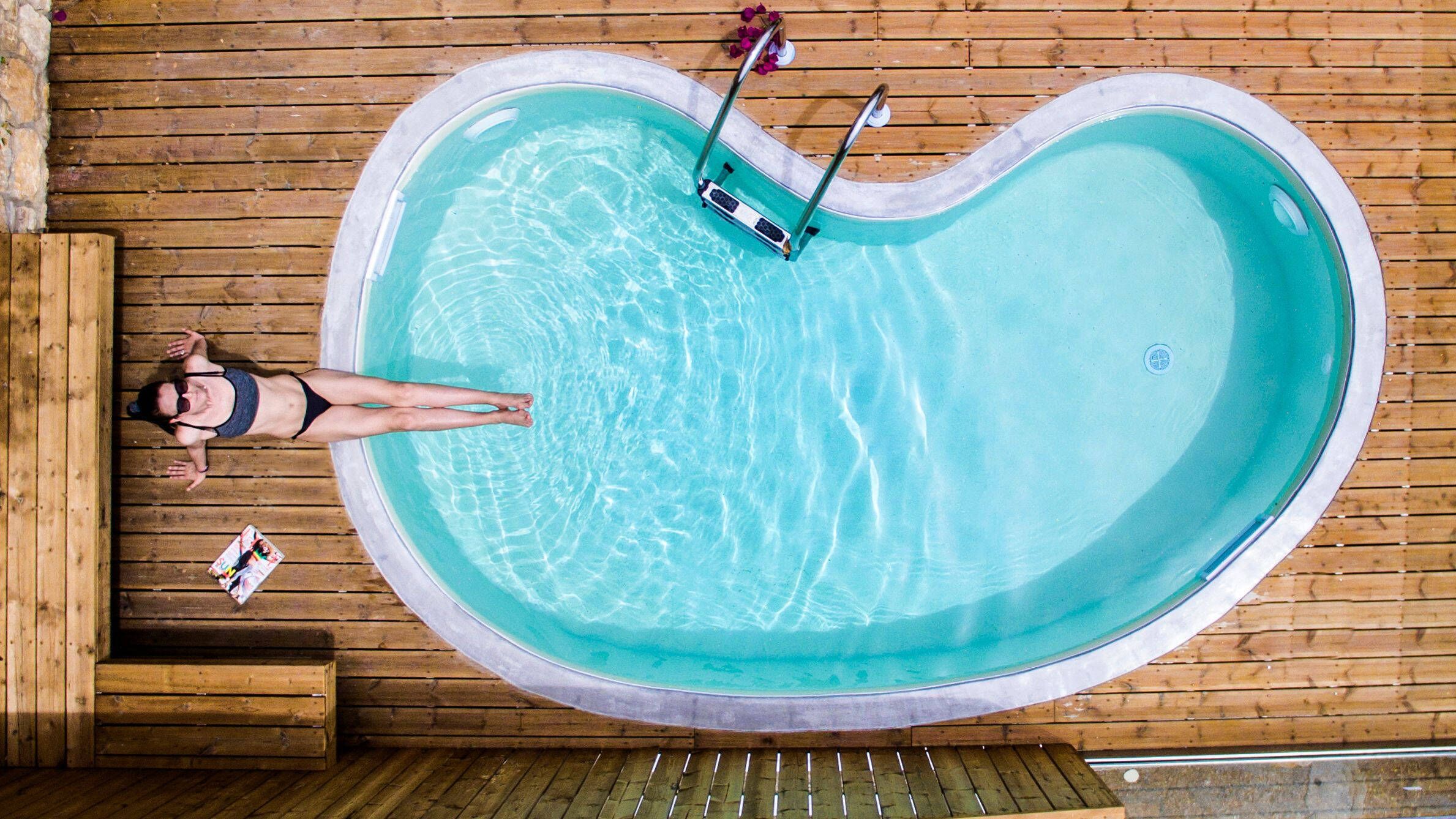 Uma pessoa em uma piscina pequena e redonda, acima do solo, com um deck de madeira ao redor.