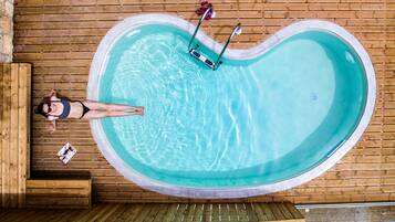 Uma pessoa em uma piscina pequena e redonda, acima do solo, com um deck de madeira ao redor.