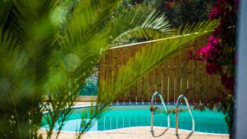 Um deck de madeira com piscina, cercado por vegetação e um muro de madeira.